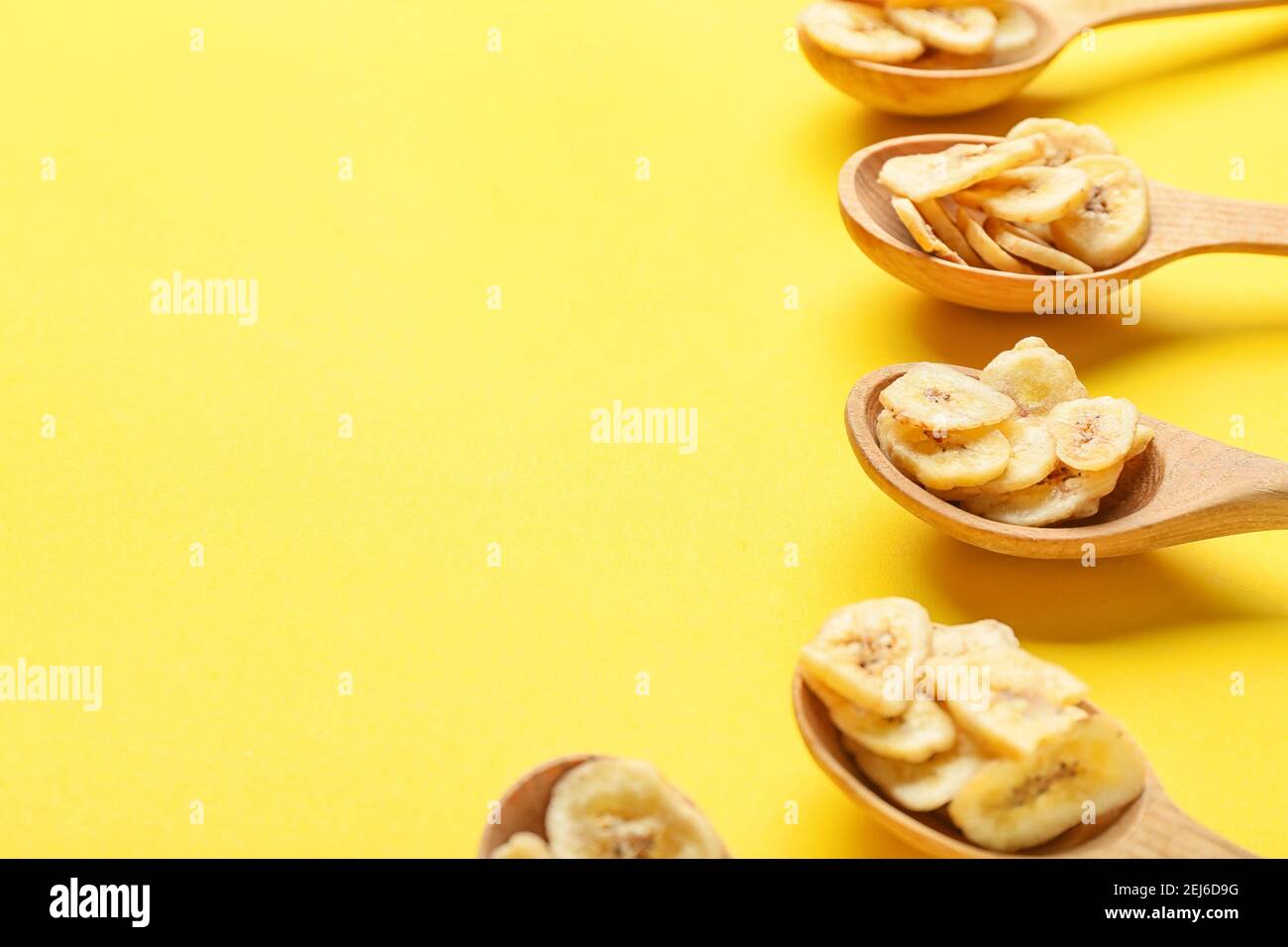 Wooden spoons with crispy banana chips on color background Stock Photo ...