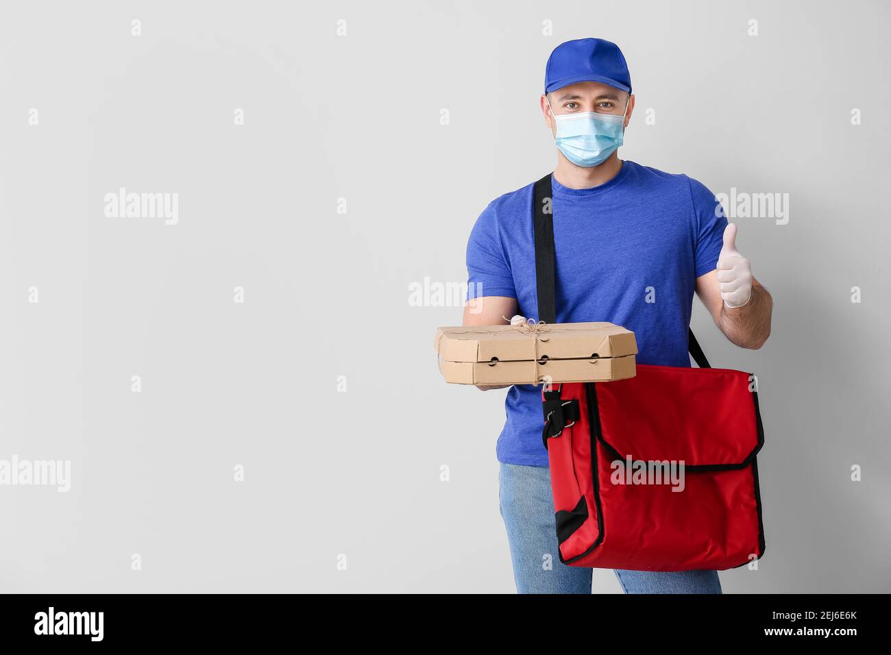 Courier of food delivery service showing thumb-up on light background ...