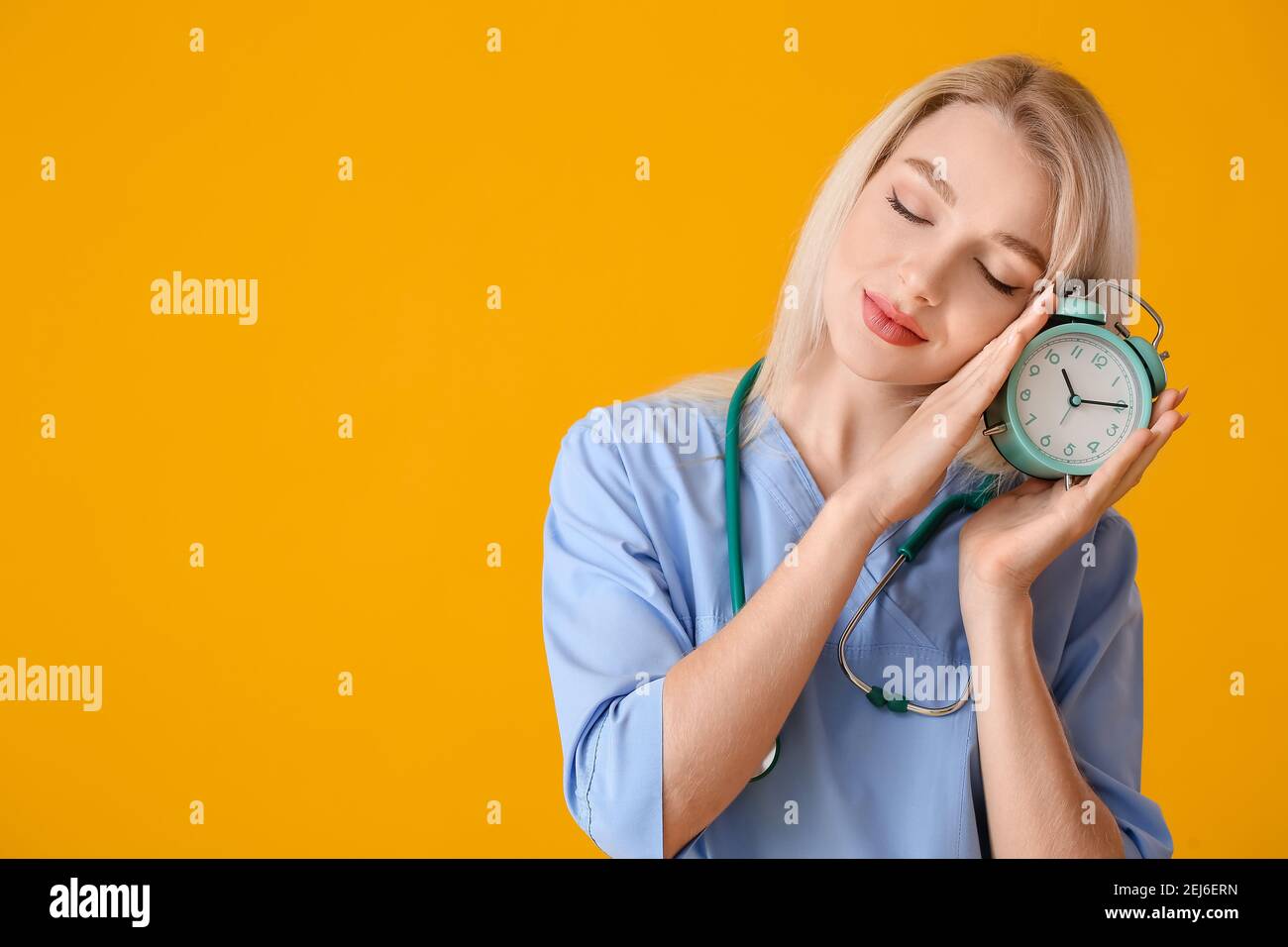 Sleepy female doctor with alarm clock on color background. Time to ...