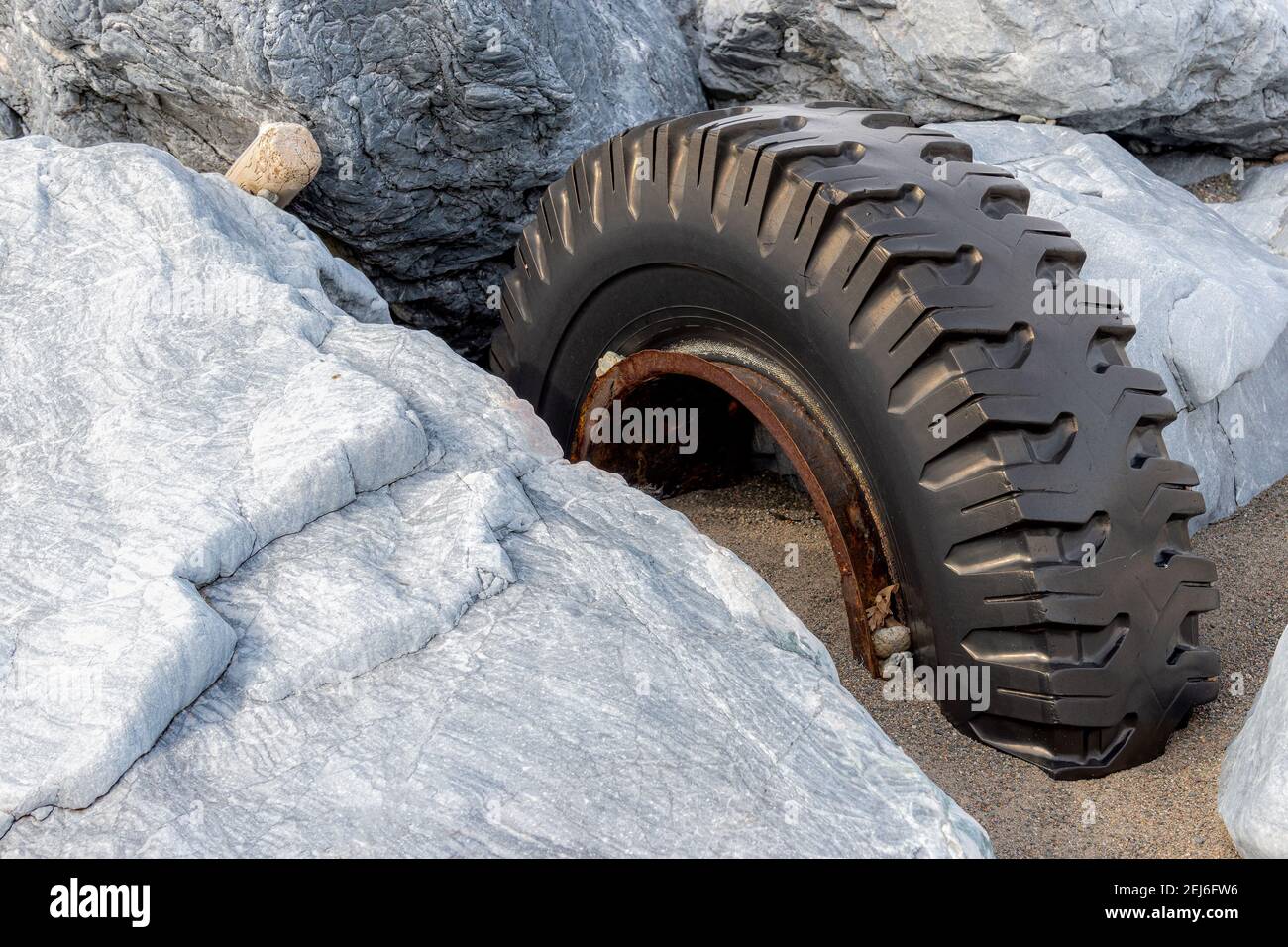 A large, worn truck tire half buried in sand between large limestone ...