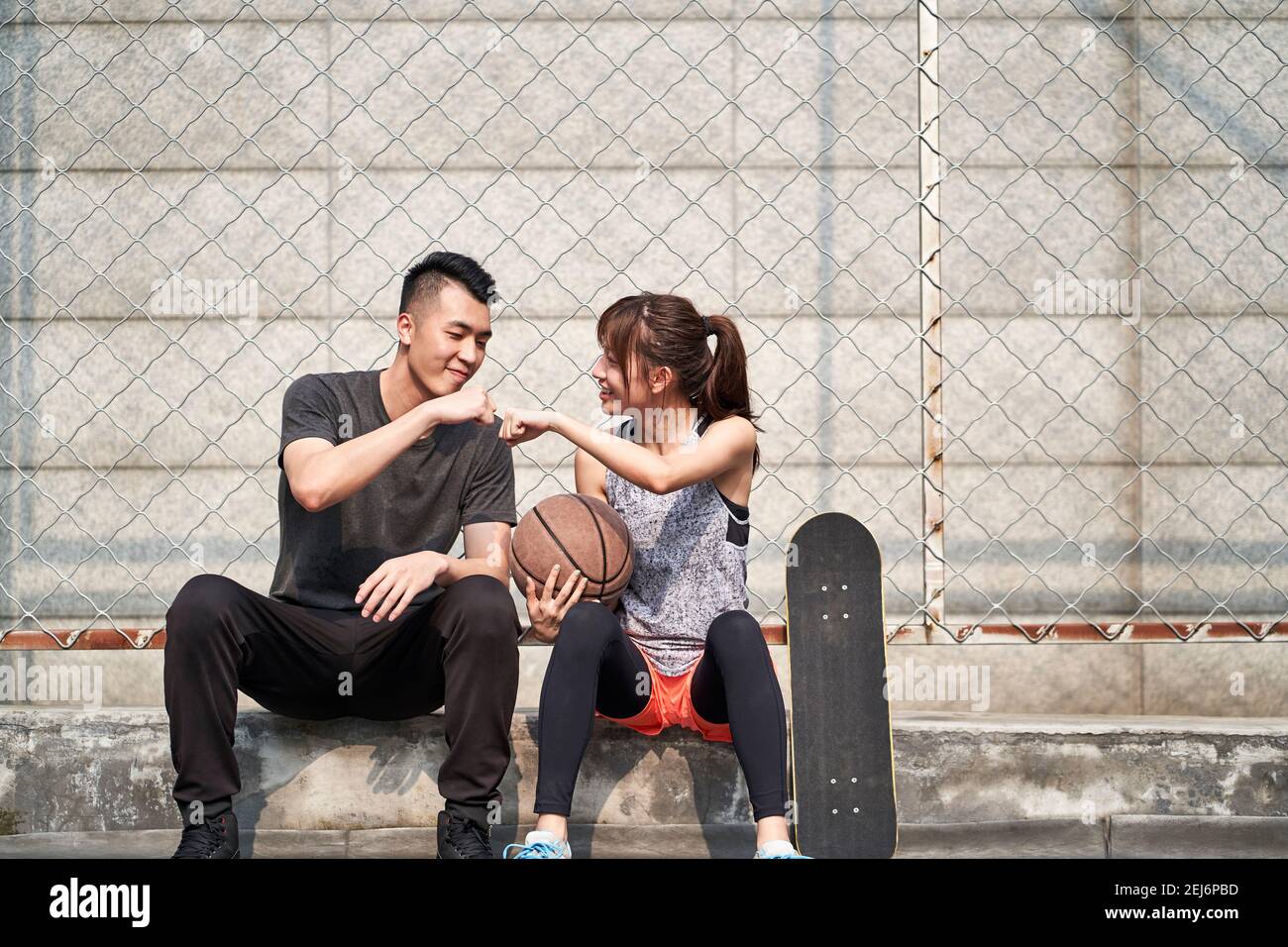 young asian adult man and woman bumping fists on a outdoor basketball ...