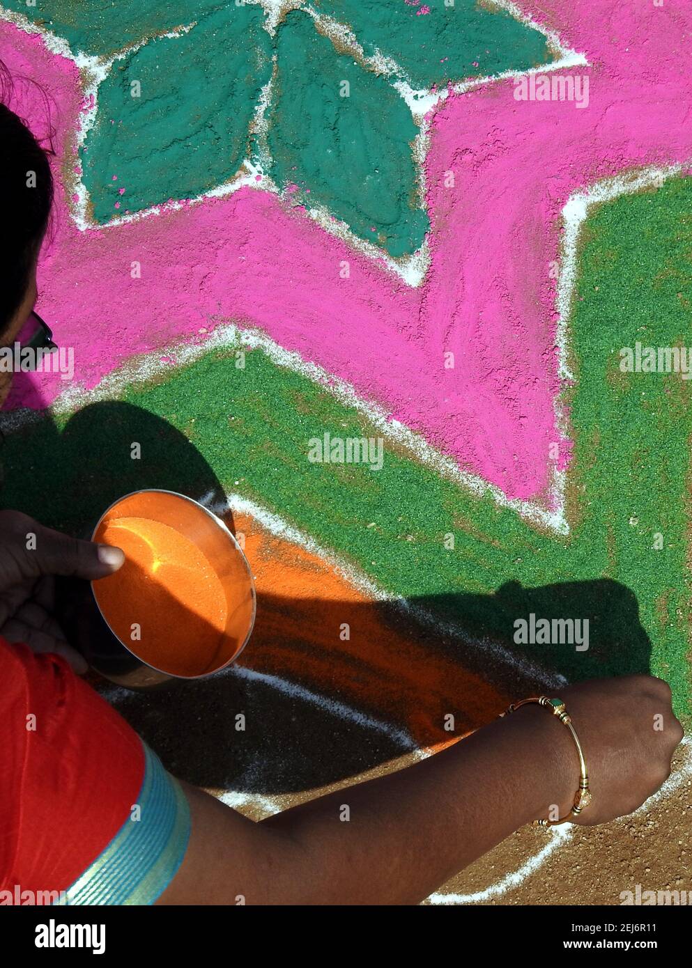 Indian woman drawing rangoli in front of house or temple during harvest ...