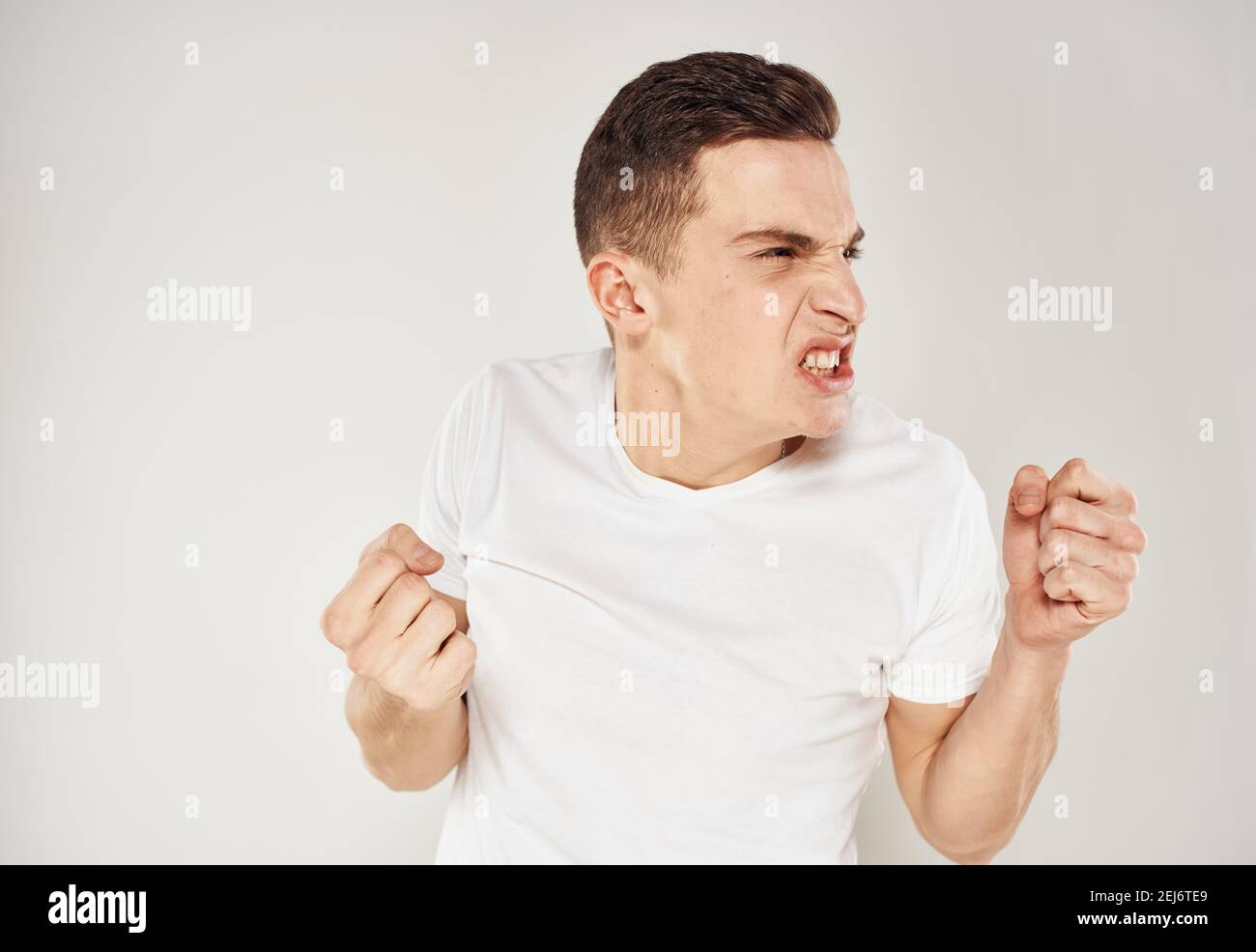 A man in a white T-shirt gestures with his hands on a gray background ...