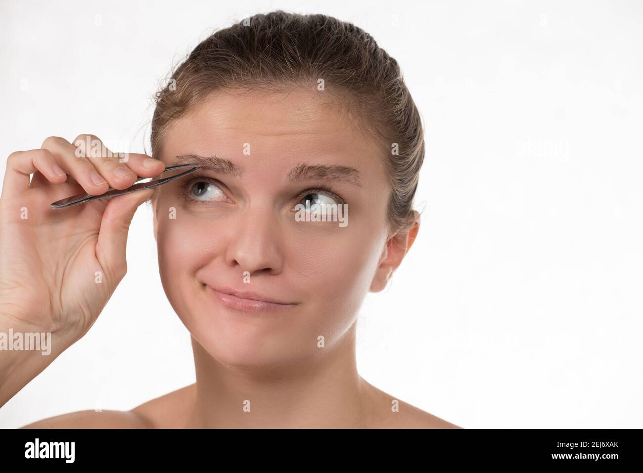 Young beautiful girl pulls out her eyebrows with tweezers metal on a ...
