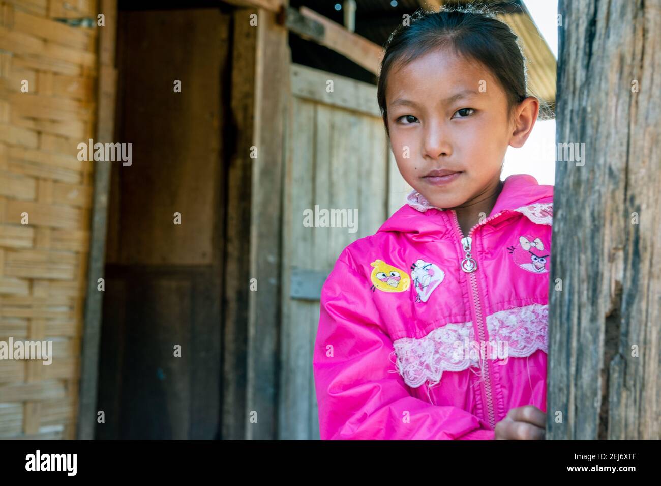 Portrait of a young asian village girl standing by her house entrance ...