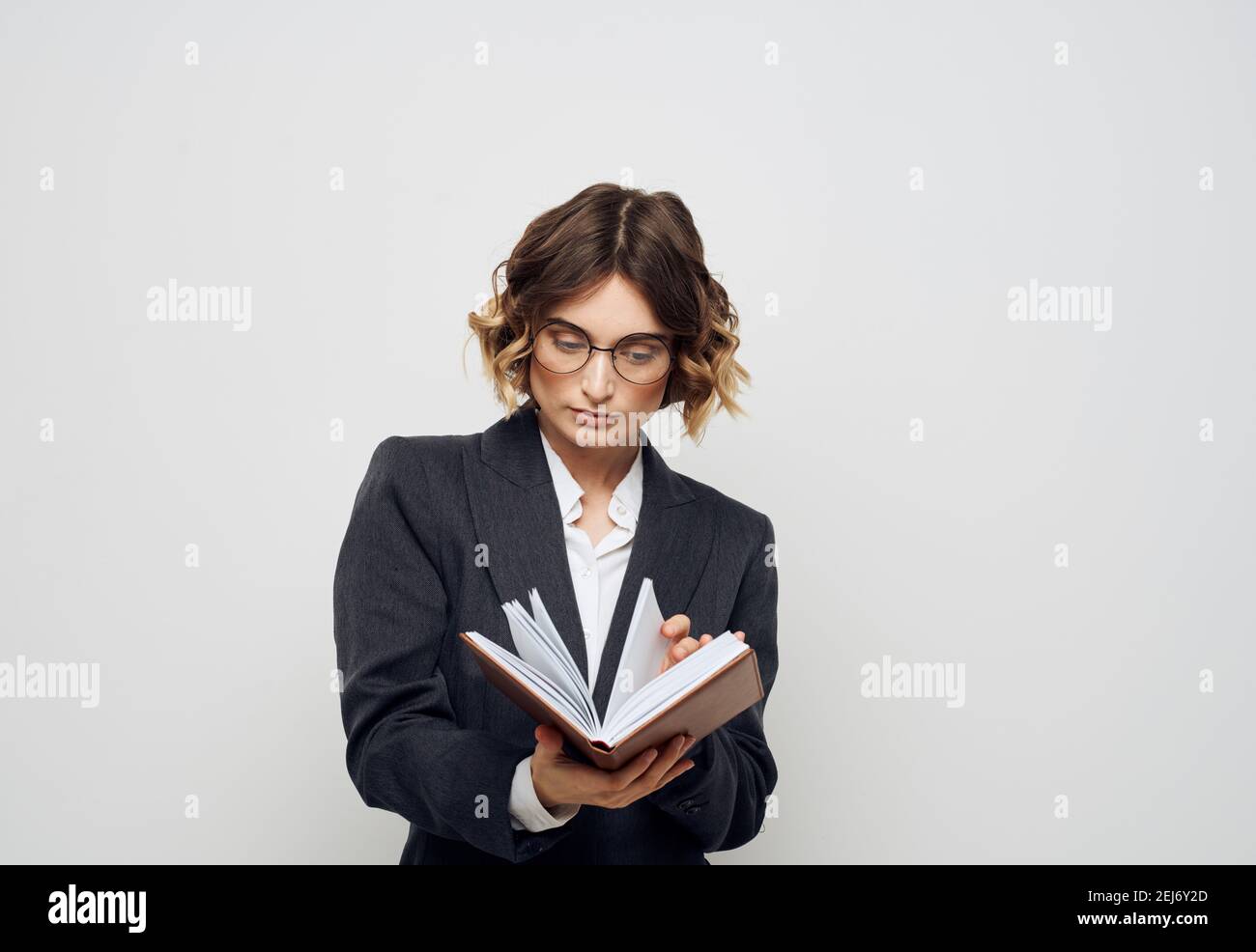 A woman in a suit with a notebook in her hands on a light background ...
