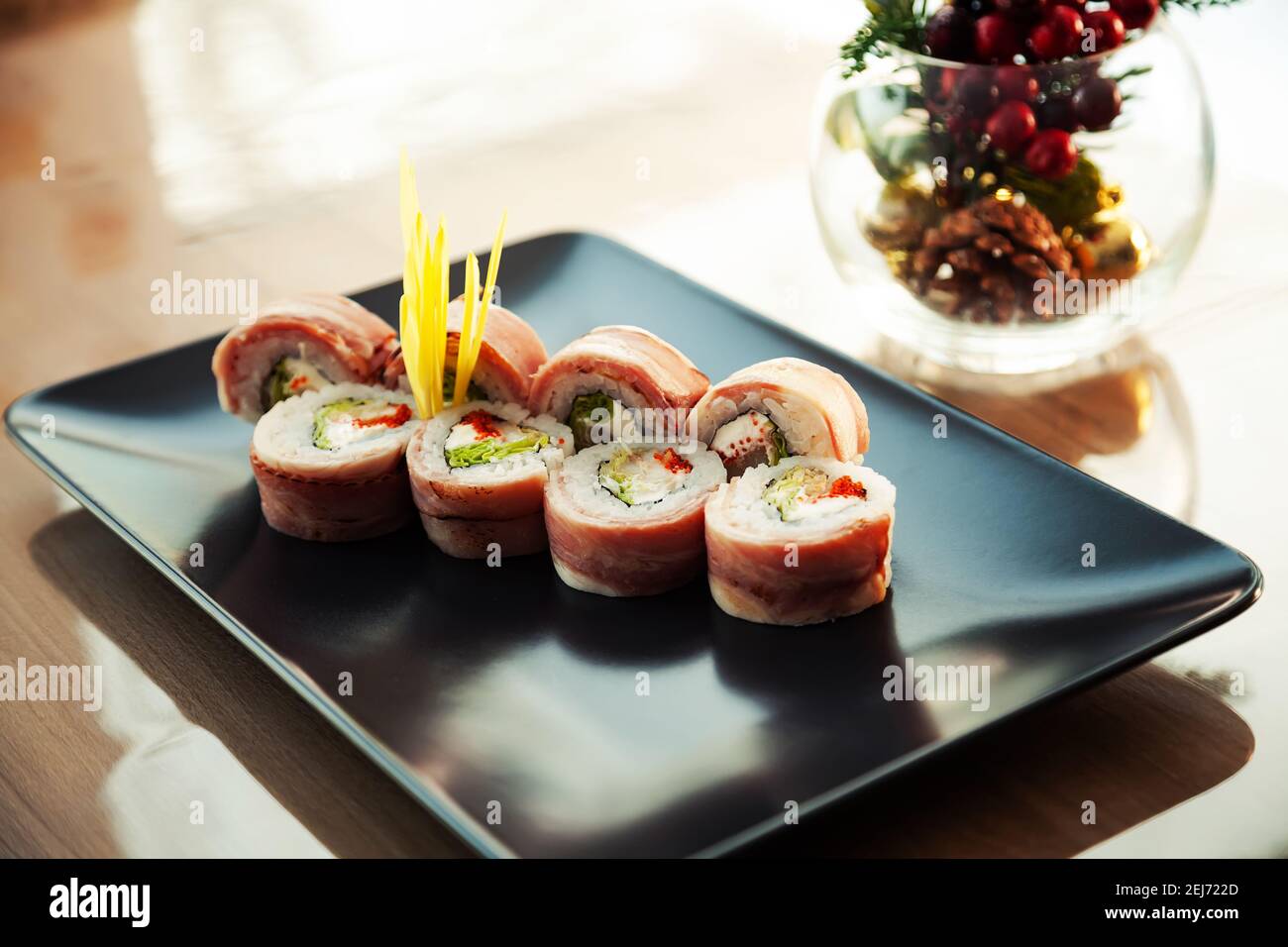 Sushi roll with bacon and fried sea bass on a black plate, ingredients ...