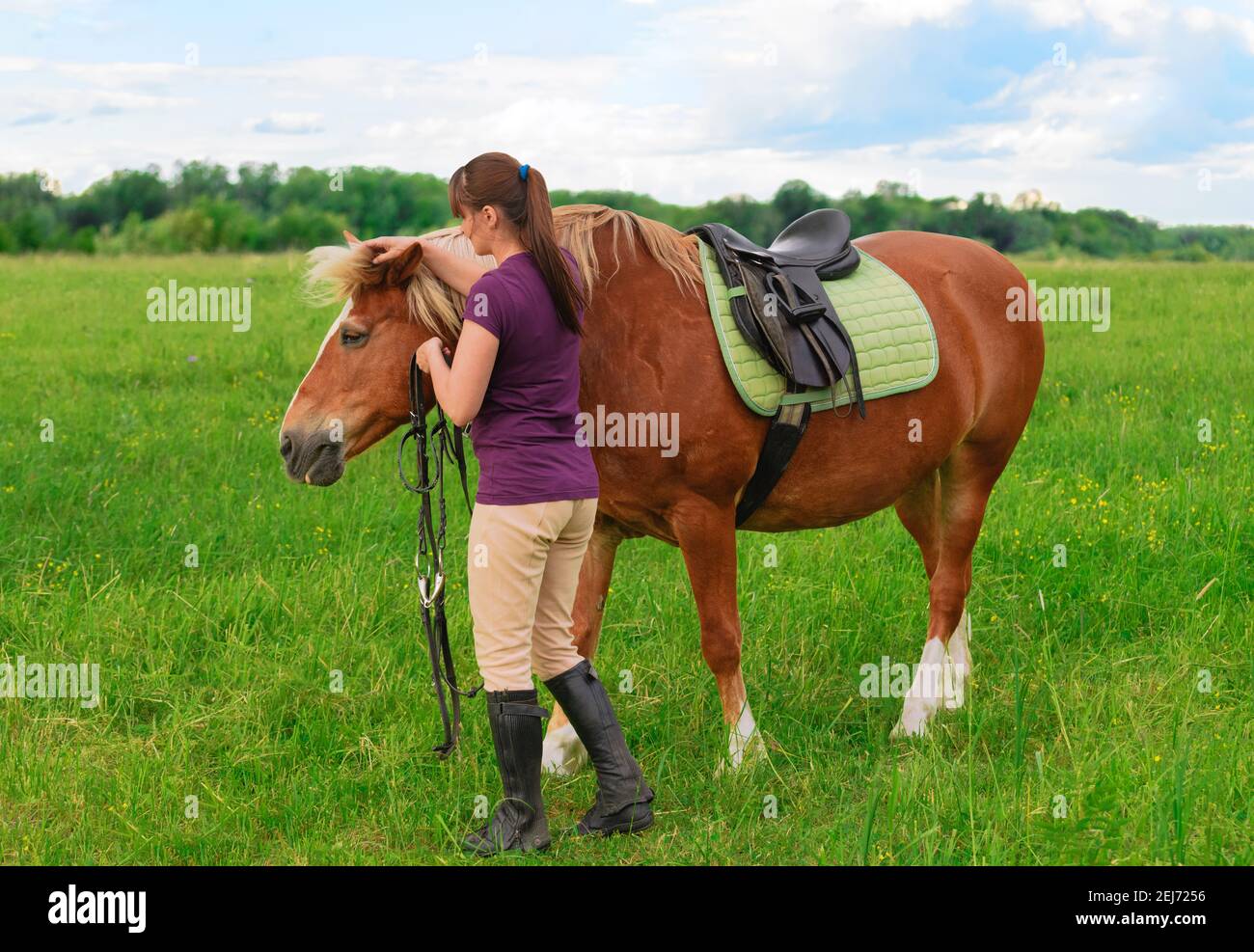 Caucasian female horse rider is standing next to her saddled mare and ...