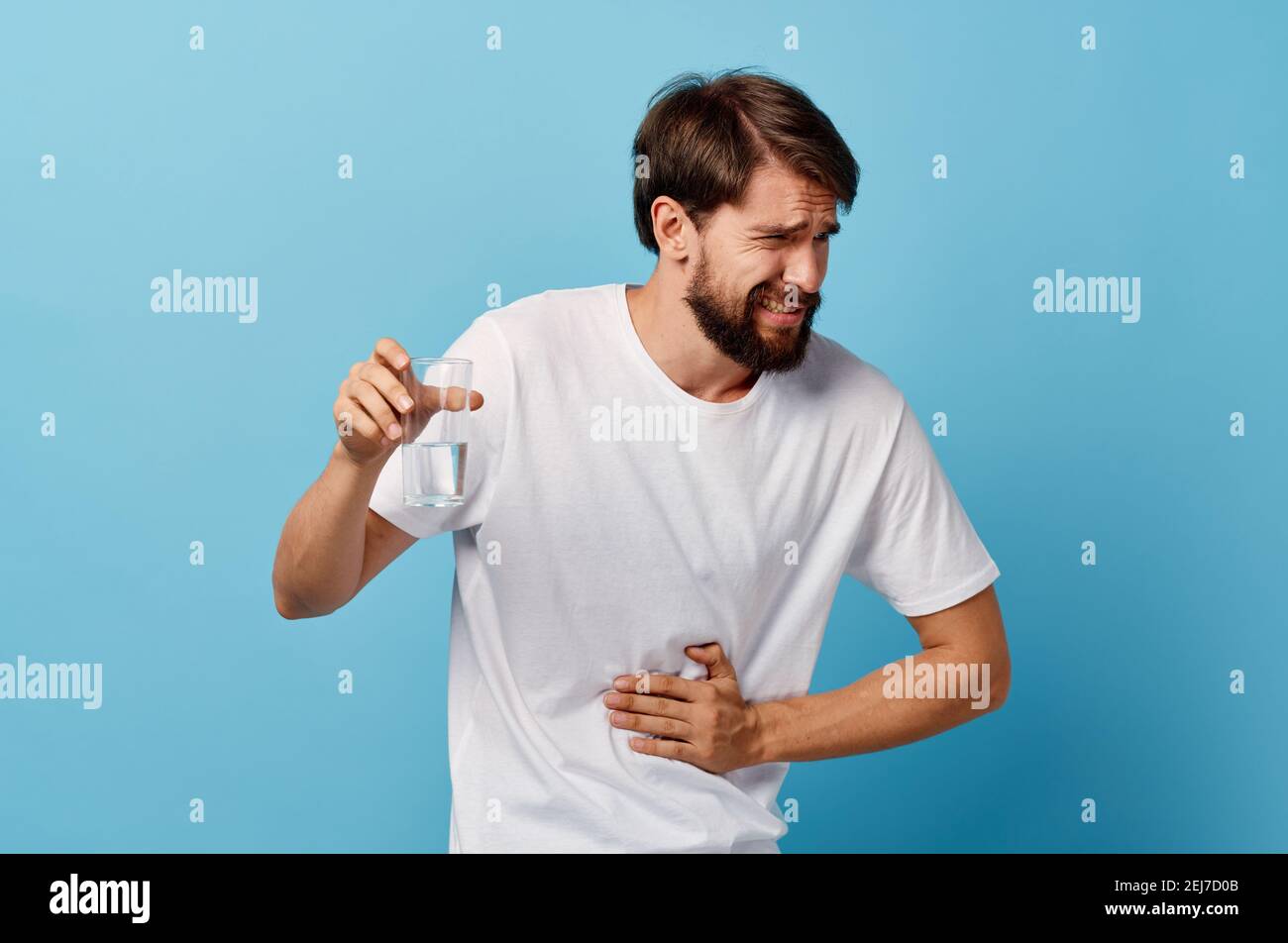a man with disgust holds a glass of water in his hand on a blue ...