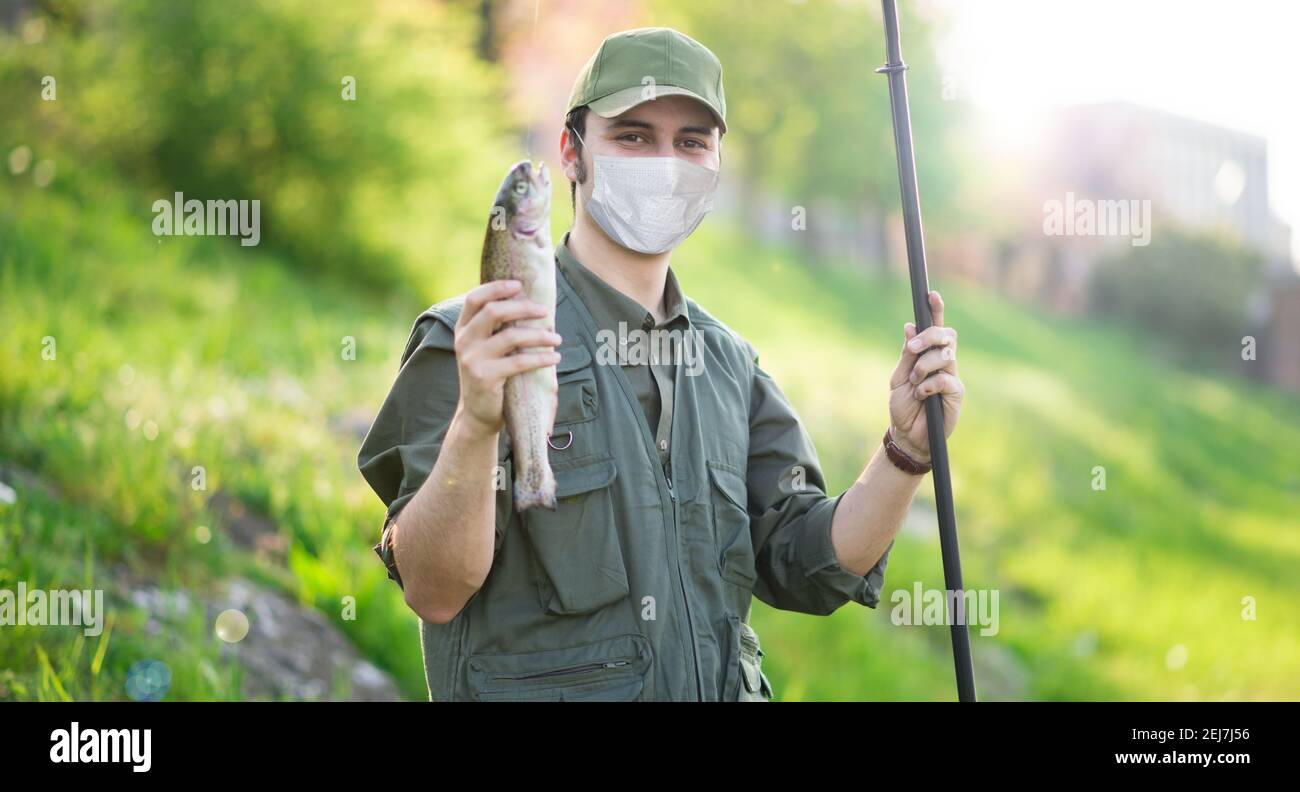 Masked fisherman showing a fish, coronavirus and covid outdoor activity ...