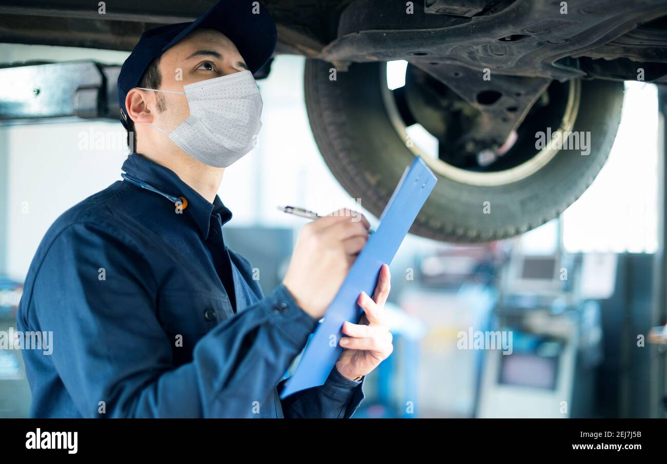 Masked car mechanic repairing a car, covid coronavirus work concept ...