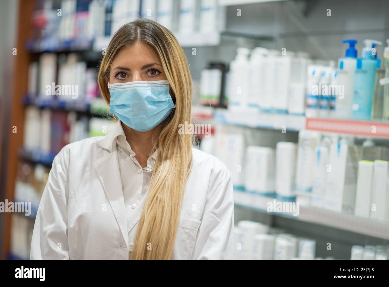 Smiling young blonde pharmacist wearing covid coronavirus mask inside ...