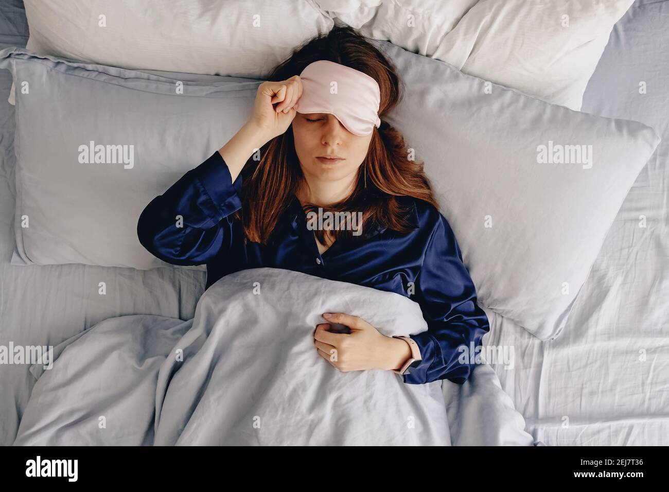 A young woman in a silk sleepwear sleeping in a bed with eyes covered ...