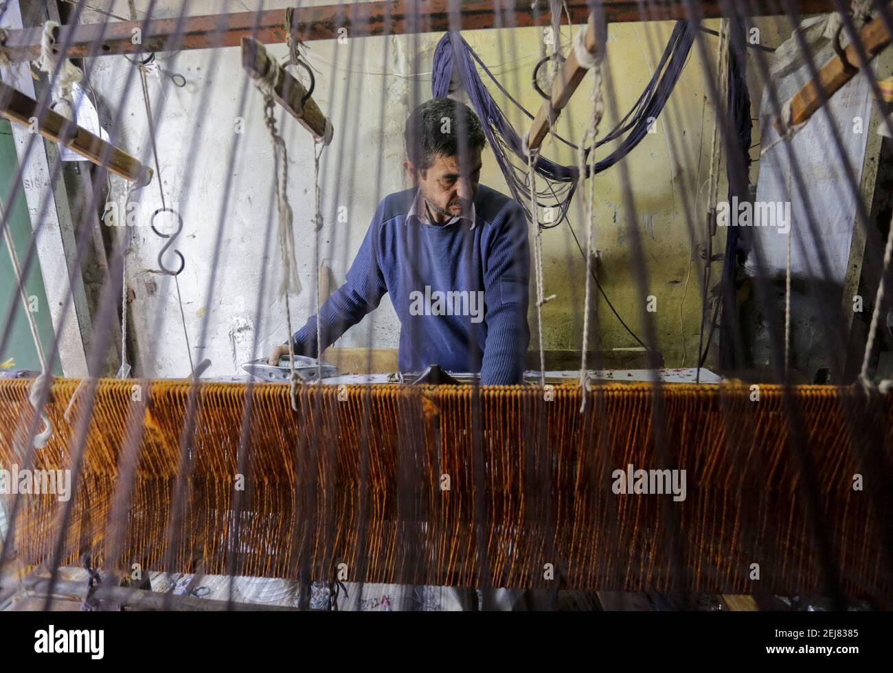 A Palestinian worker weaves carpets on a traditional wooden loom at a ...