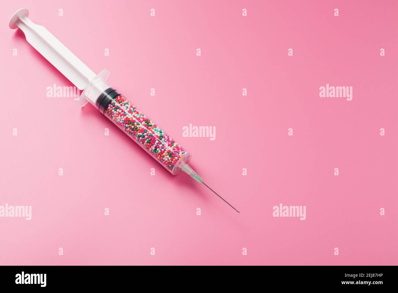 Medical Syringe filled with colorful balloons on a pink background with ...