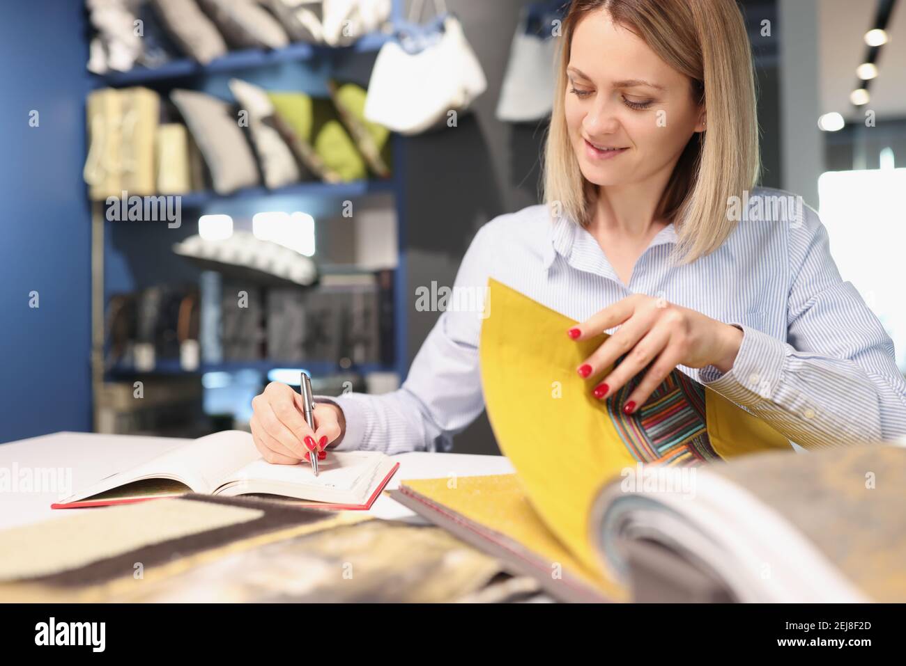 Woman writing with pen in notebook and leafing through catalog with ...