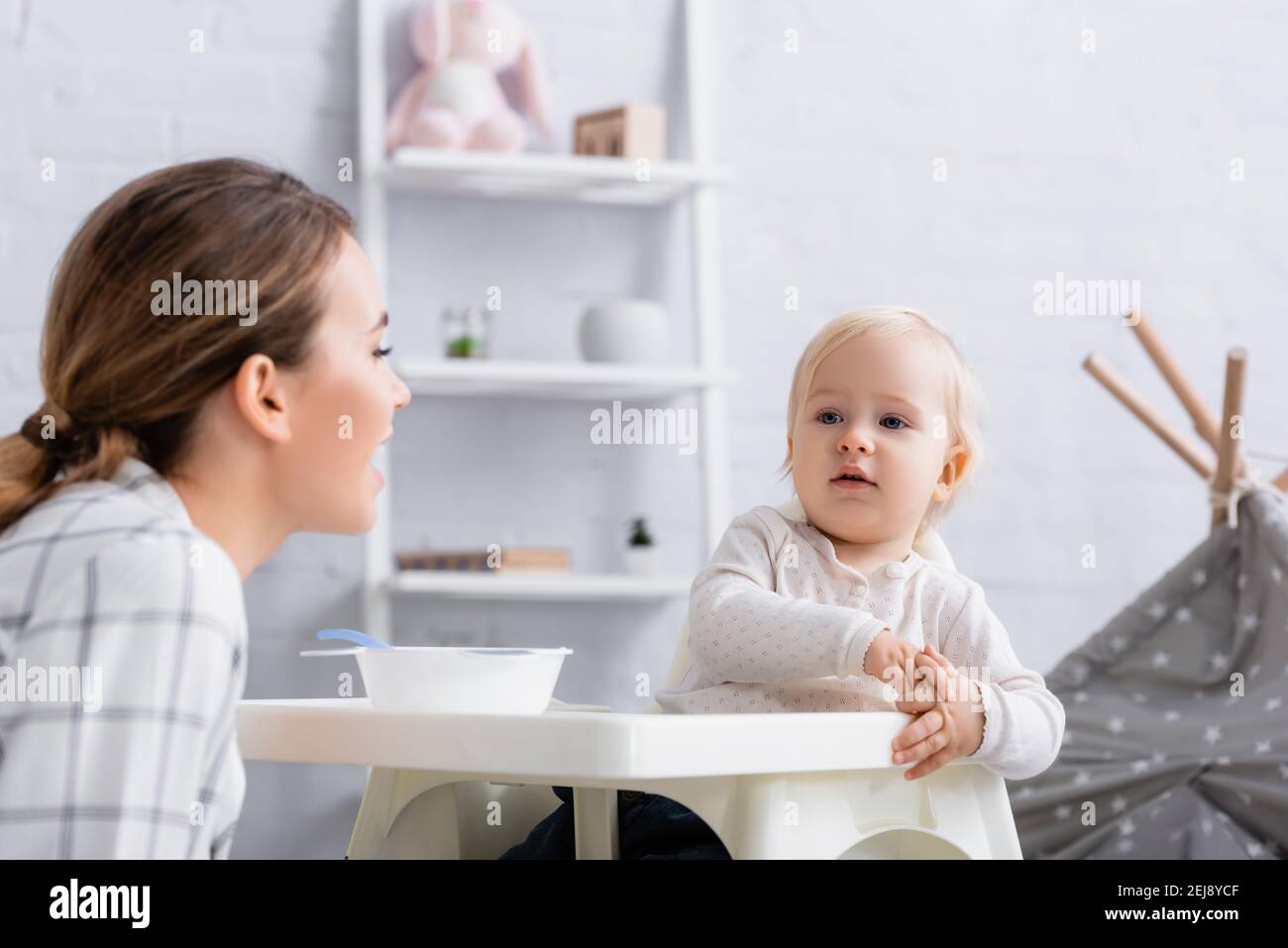 young woman looking at little son sitting on kids chair near bowl ...
