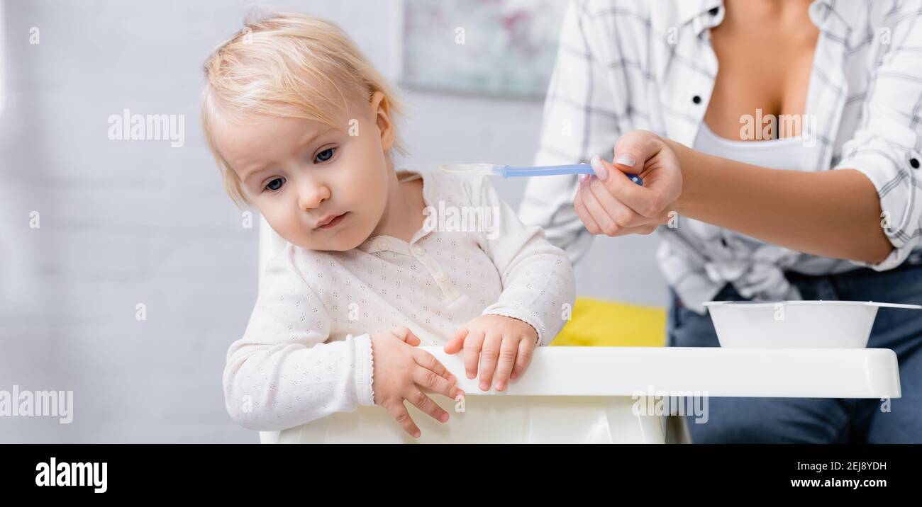toddler boy turning away from spoon with puree in hand of mother ...