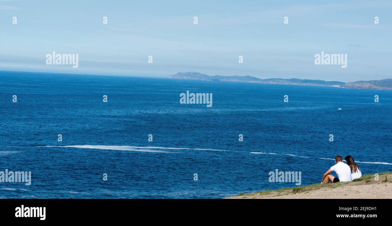 Couple sitting on the shore looking at the blue sea from a cliff Stock ...