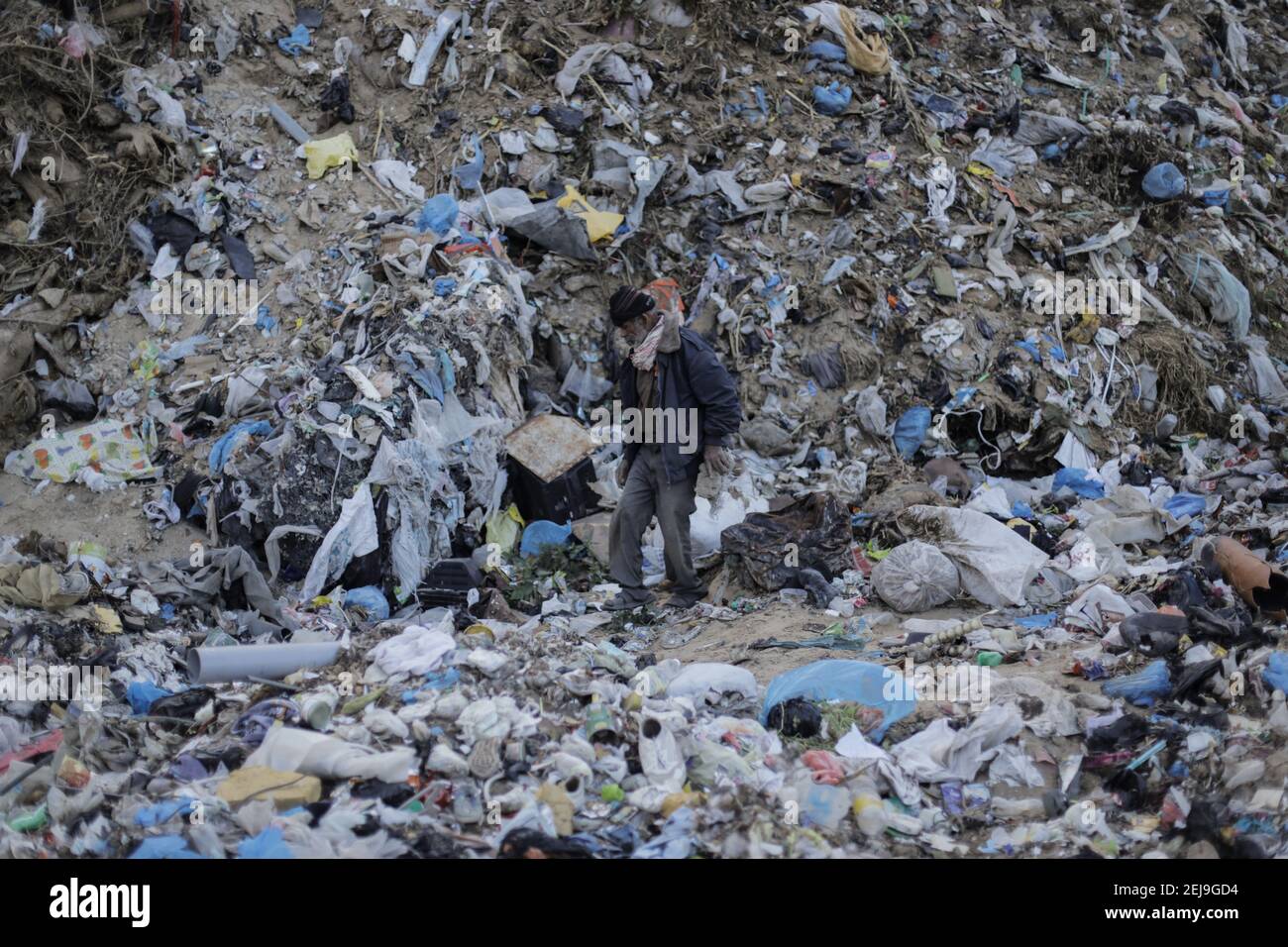 A man walks over plastic waste during a cold weather spell in a slum on ...