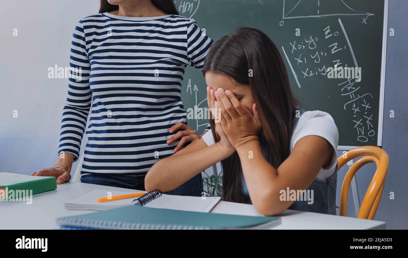 mother standing near crying daughter covering face while doing homework ...