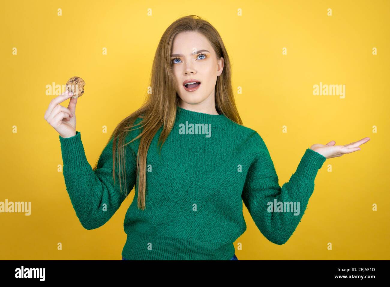 Young beautiful woman eating chocolate cookie over yellow background ...