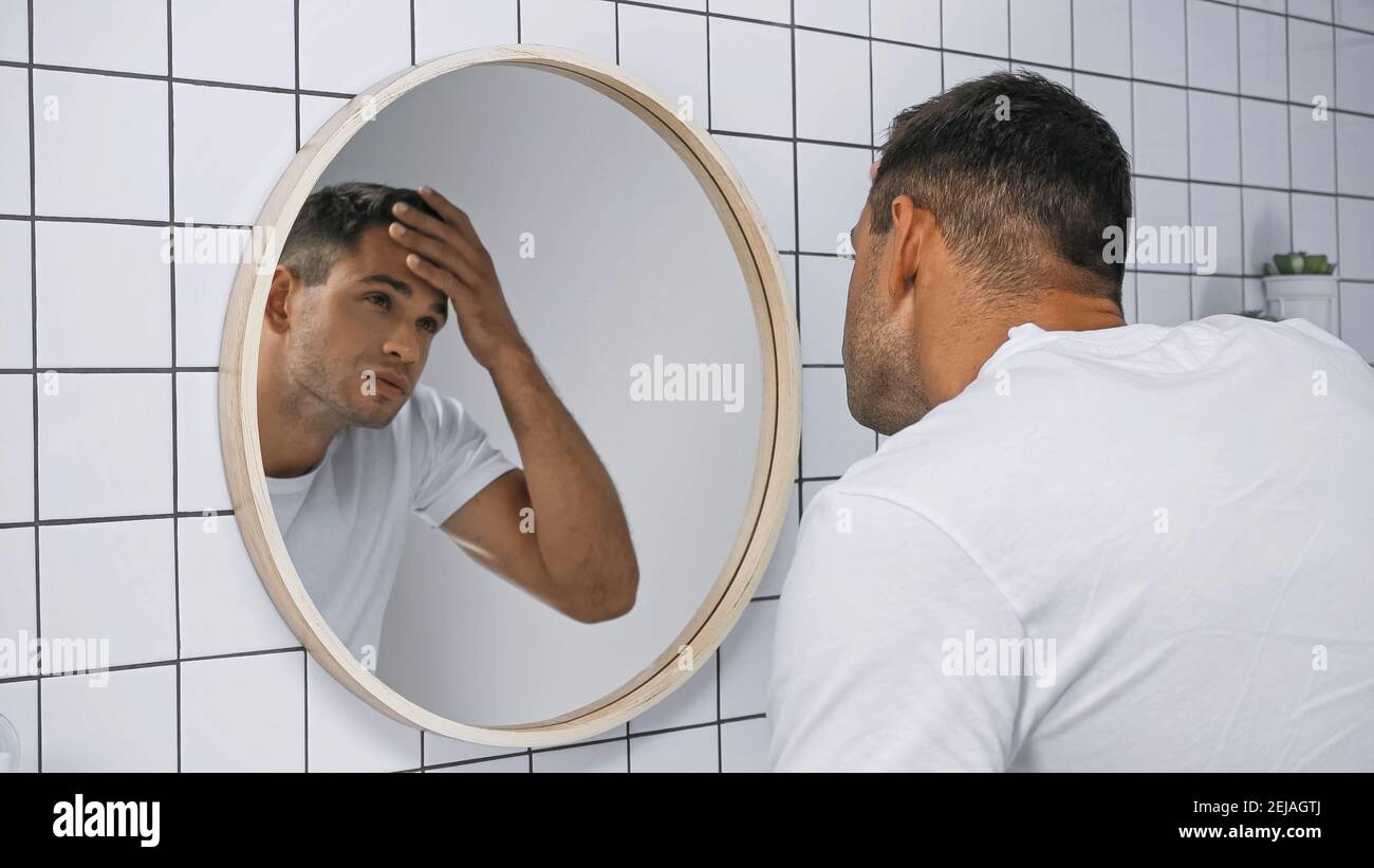 young man touching forehead while looking at mirror in bathroom Stock ...