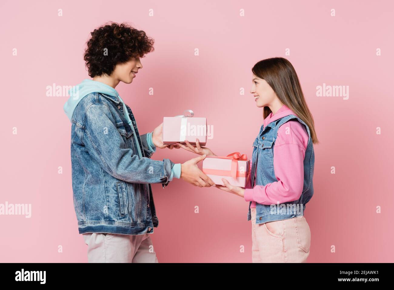 Side view of smiling teenagers giving presents to each other isolated ...