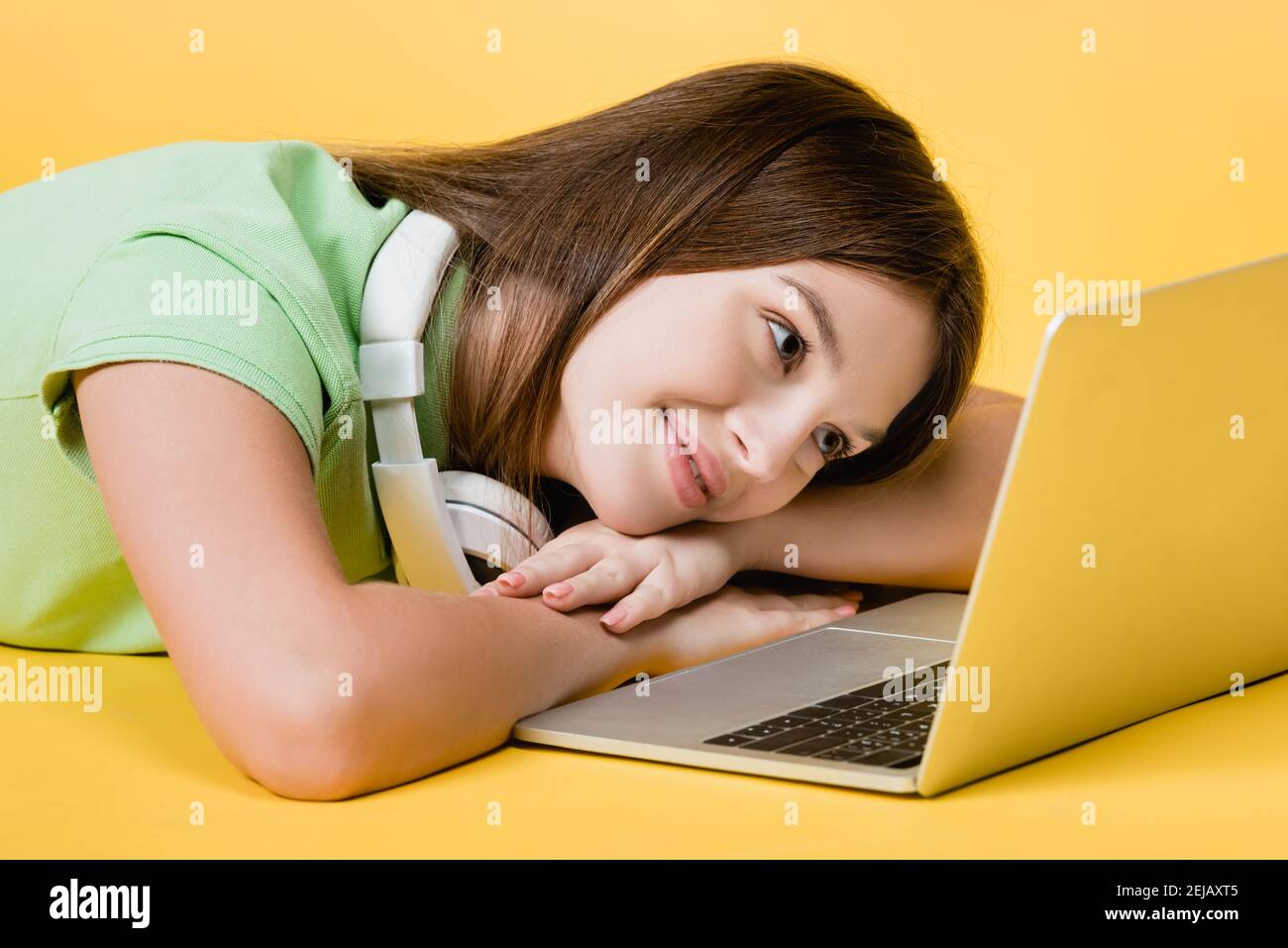 Smiling teenage girl looking at laptop on yellow background Stock Photo ...
