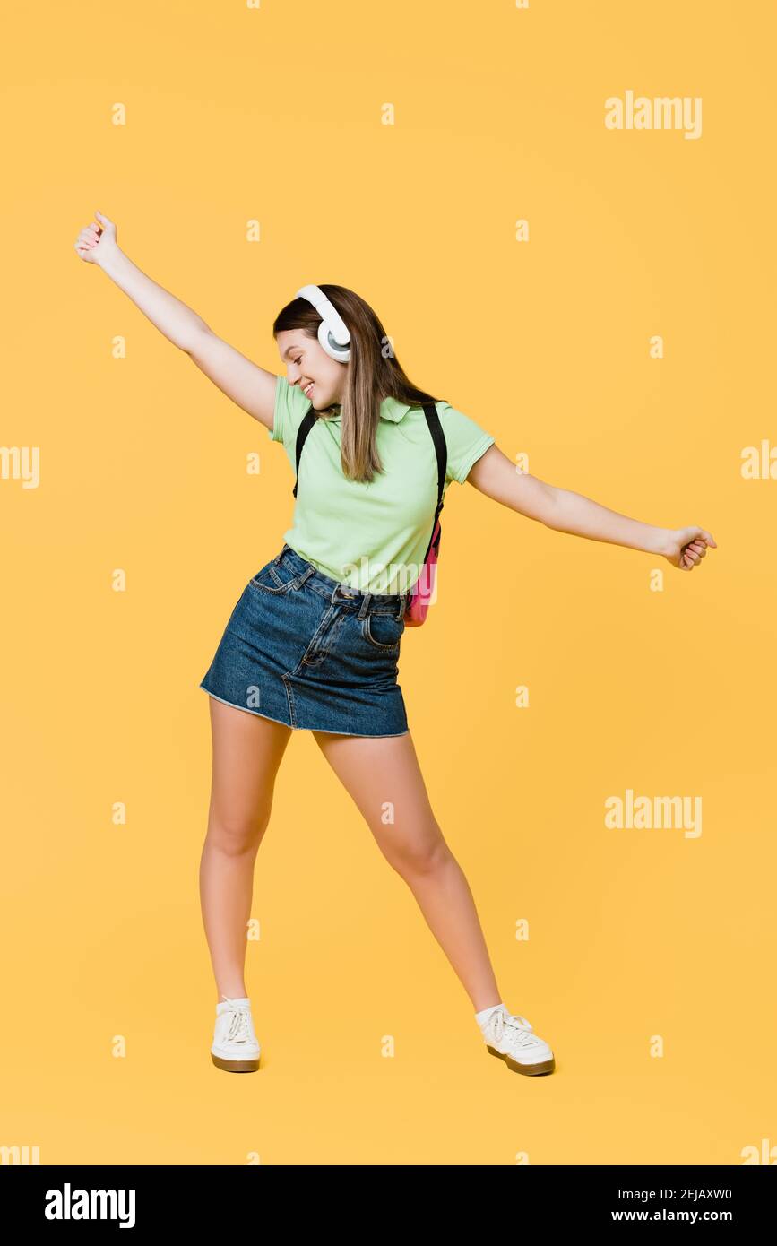 Positive teen girl in headphones with backpack dancing isolated on ...