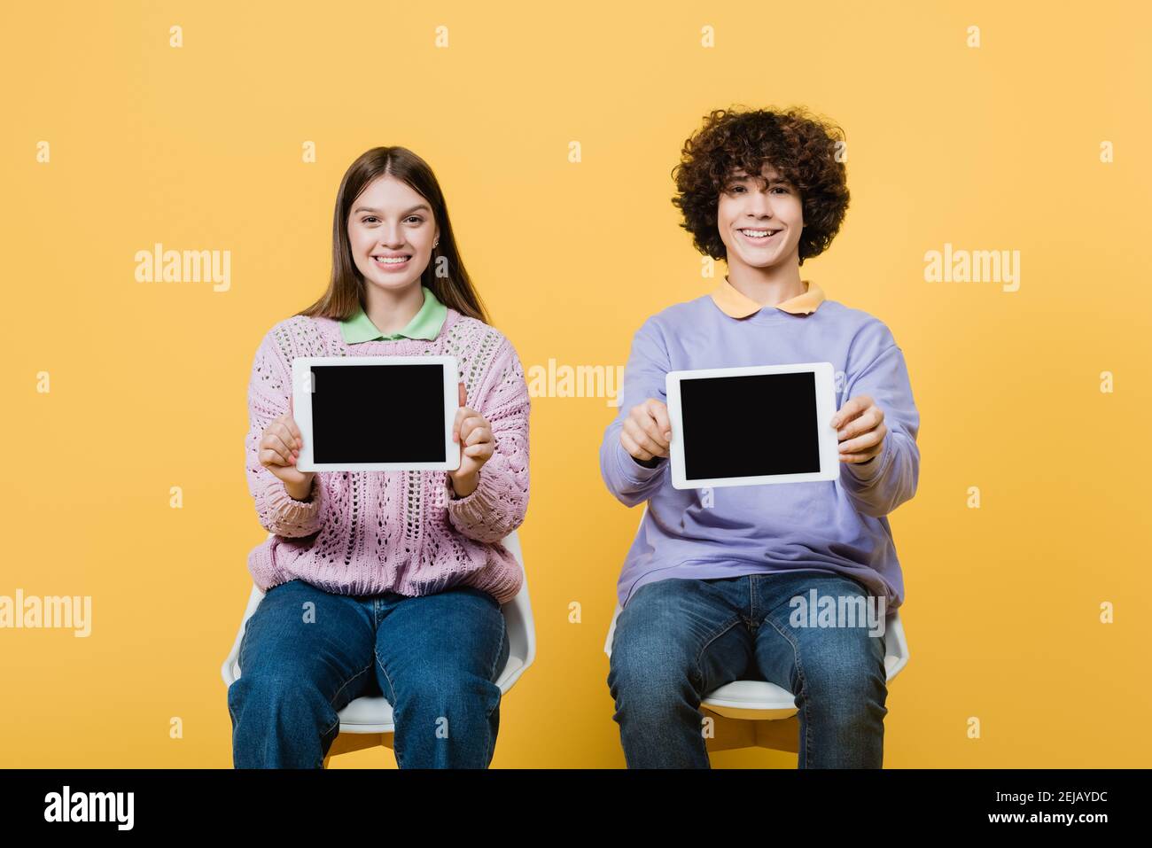 Positive teenagers showing digital tablets on yellow background Stock ...