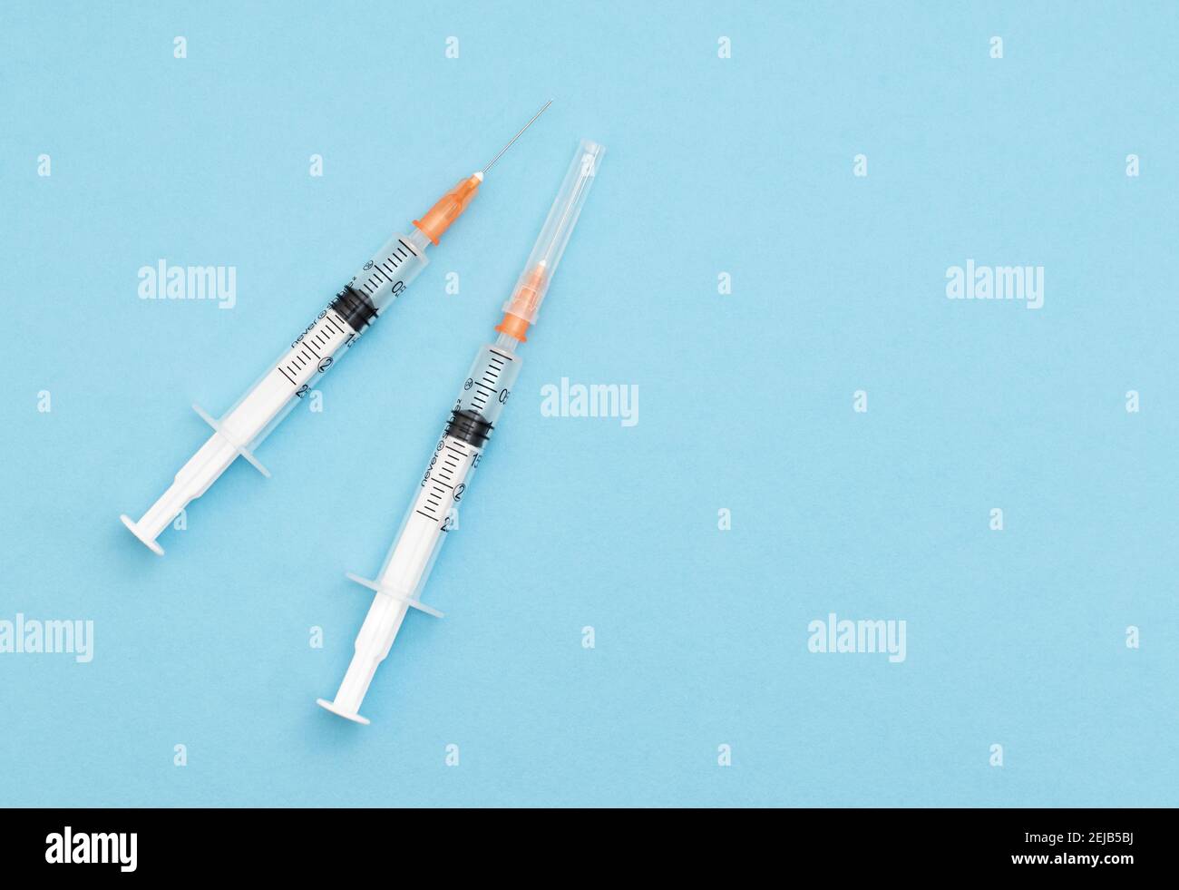 Two syringes with needles on a light blue background, with copy space ...