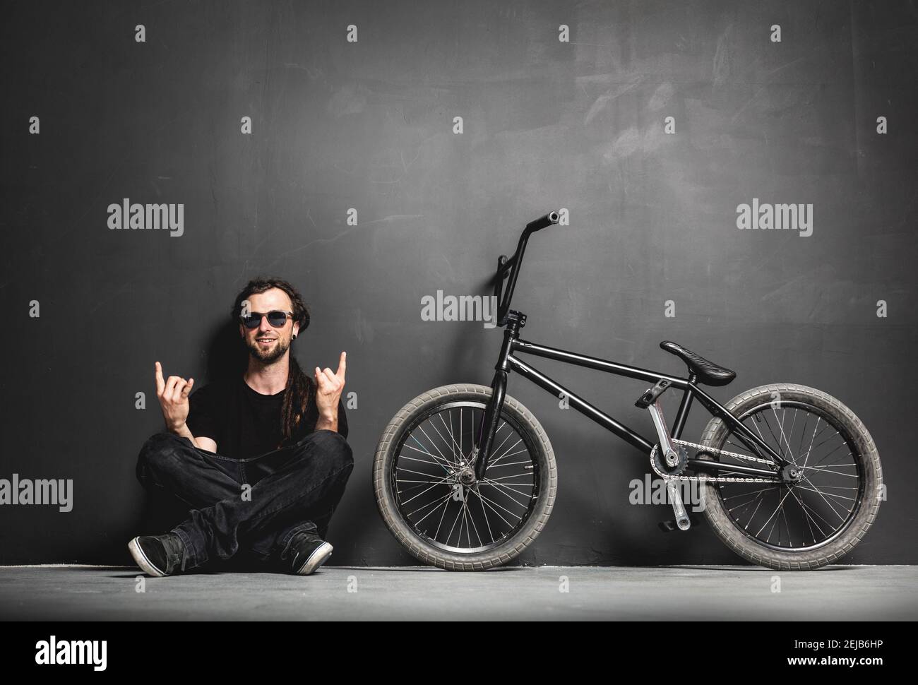Happy man sitting next to his BMX bike, showing rocker gesture. Chill ...