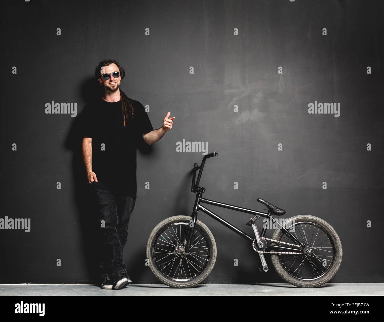 Man standing next to his BMX bike, pointing his finger. Dreadlocks and ...