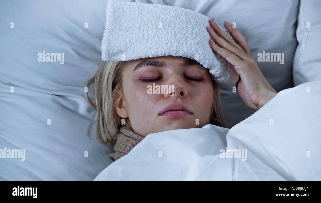 diseased woman lying with closed eyes and touching compress on forehead ...