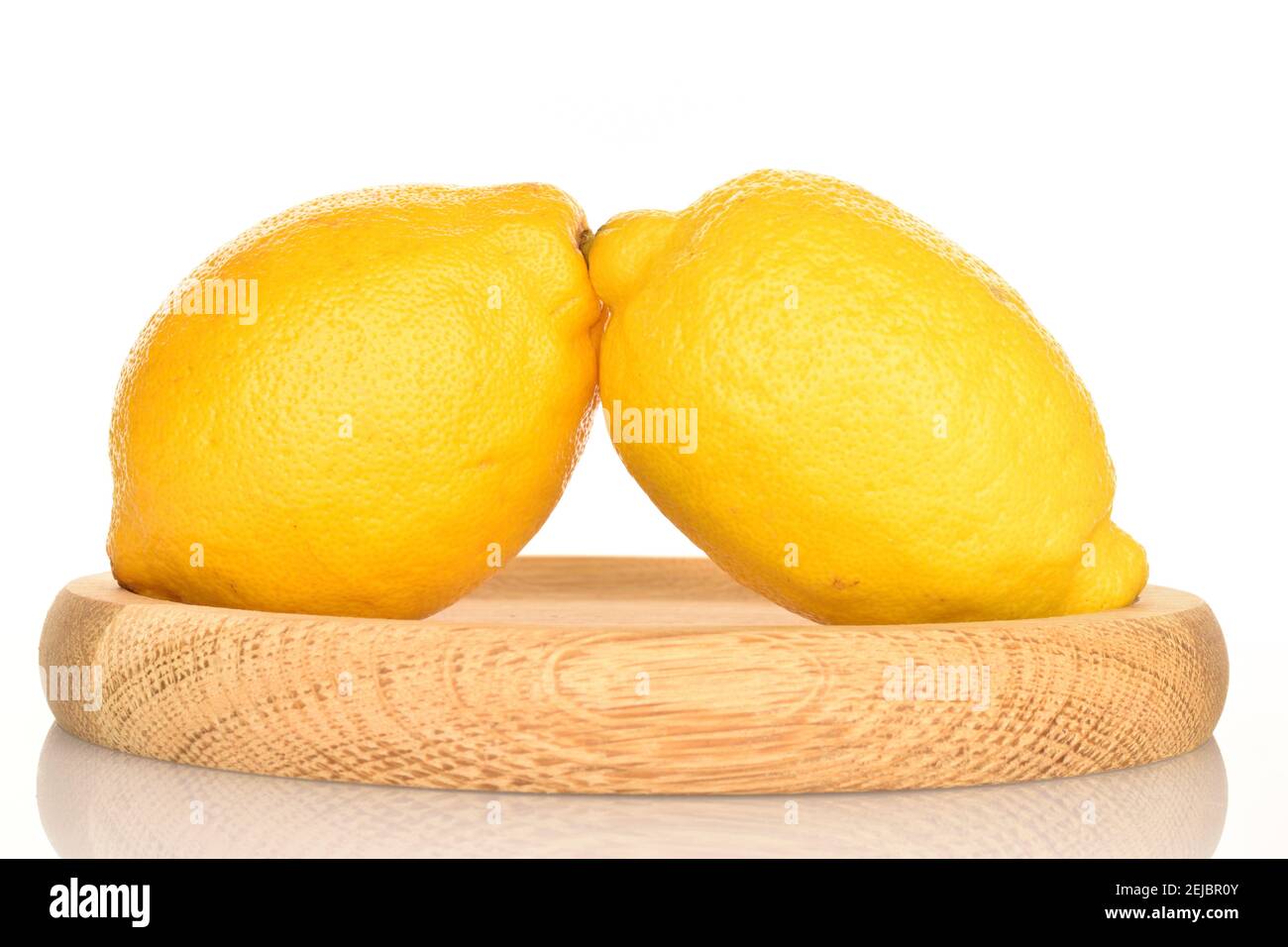 Two whole bright yellow ripe tasty organic lemons on a round wooden ...