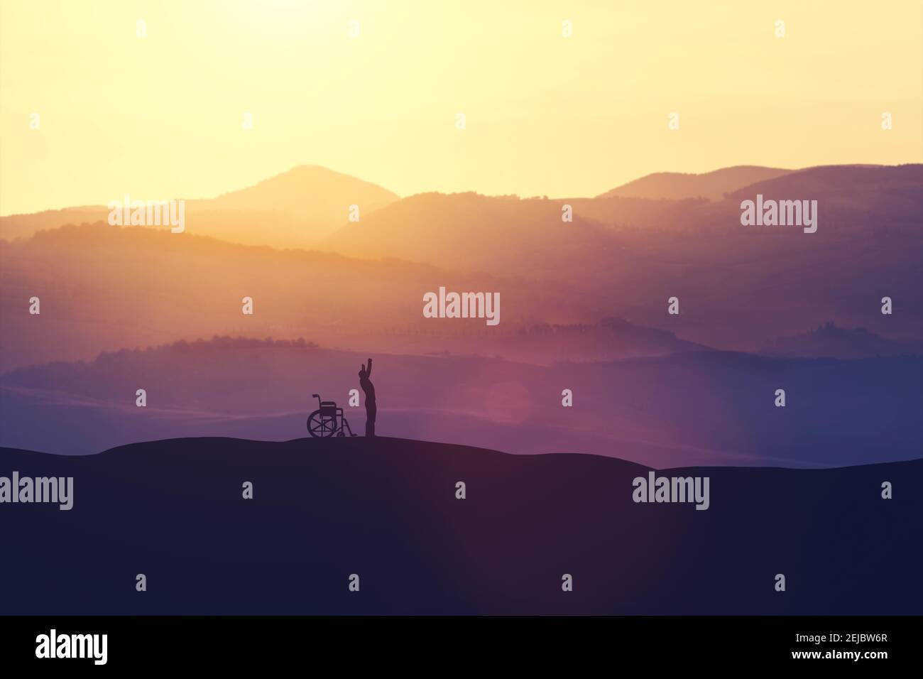 Happy man getting up from a wheelchair on a hill during sunset ...