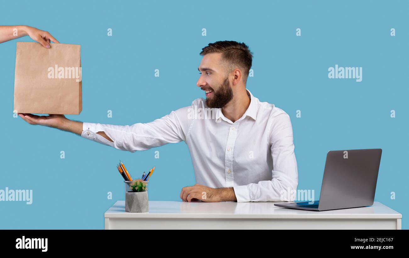 Young man receiving food delivery from courier at office, blue studio ...