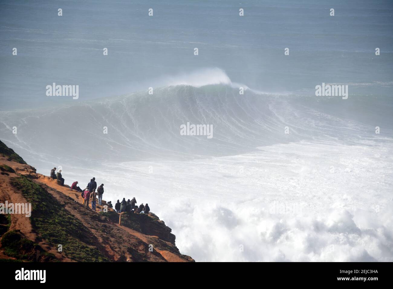 Small crowd watching big waves from the cliffs of Nazare Portugal Stock ...