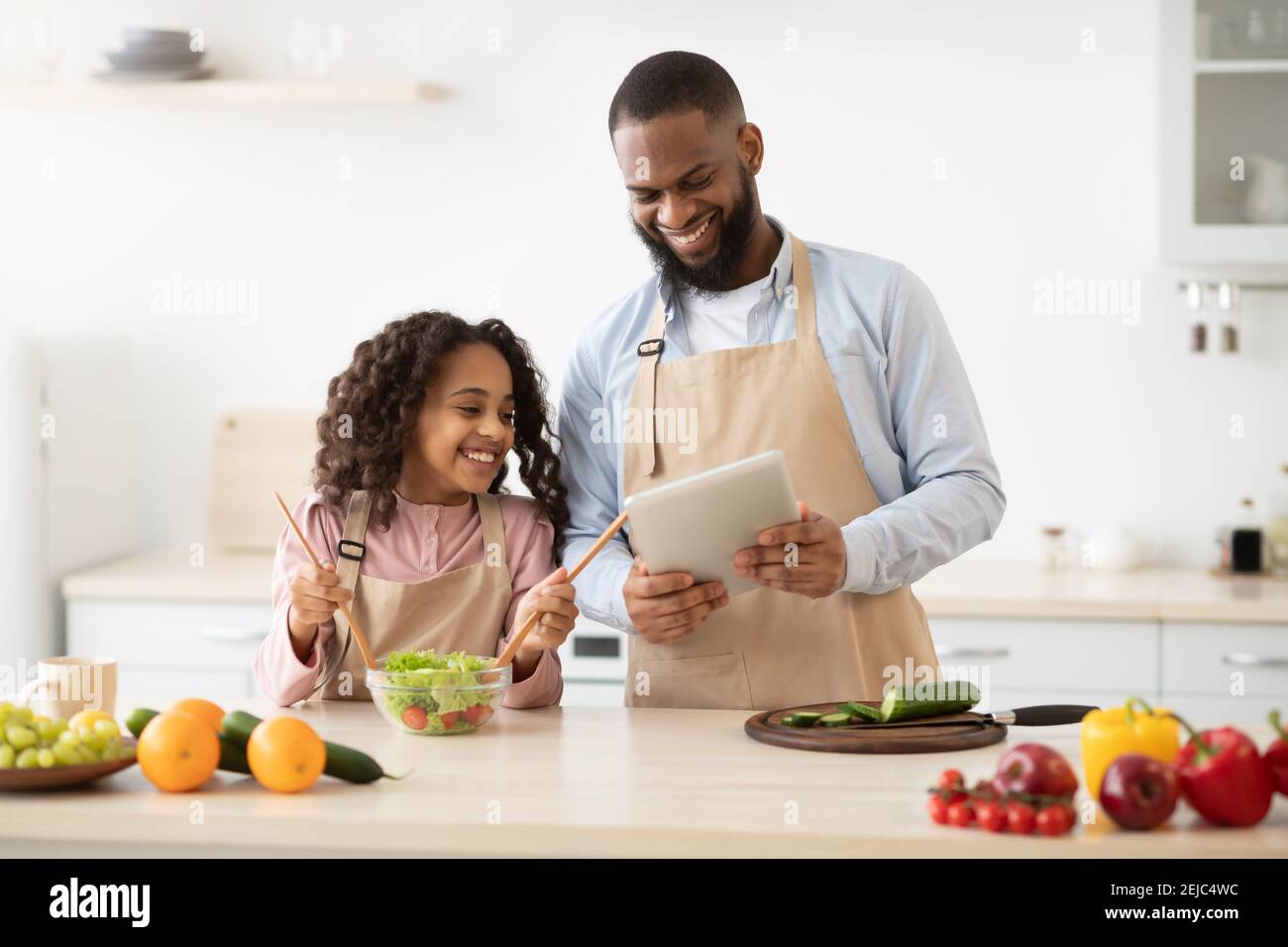 Black man and girl cooking in the kitchen reading recipe Stock Photo ...