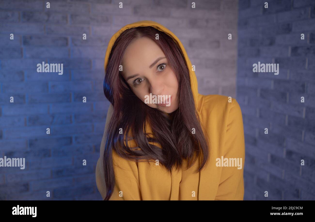 Portrait of shy young woman in hood on backlit background. Close up of ...