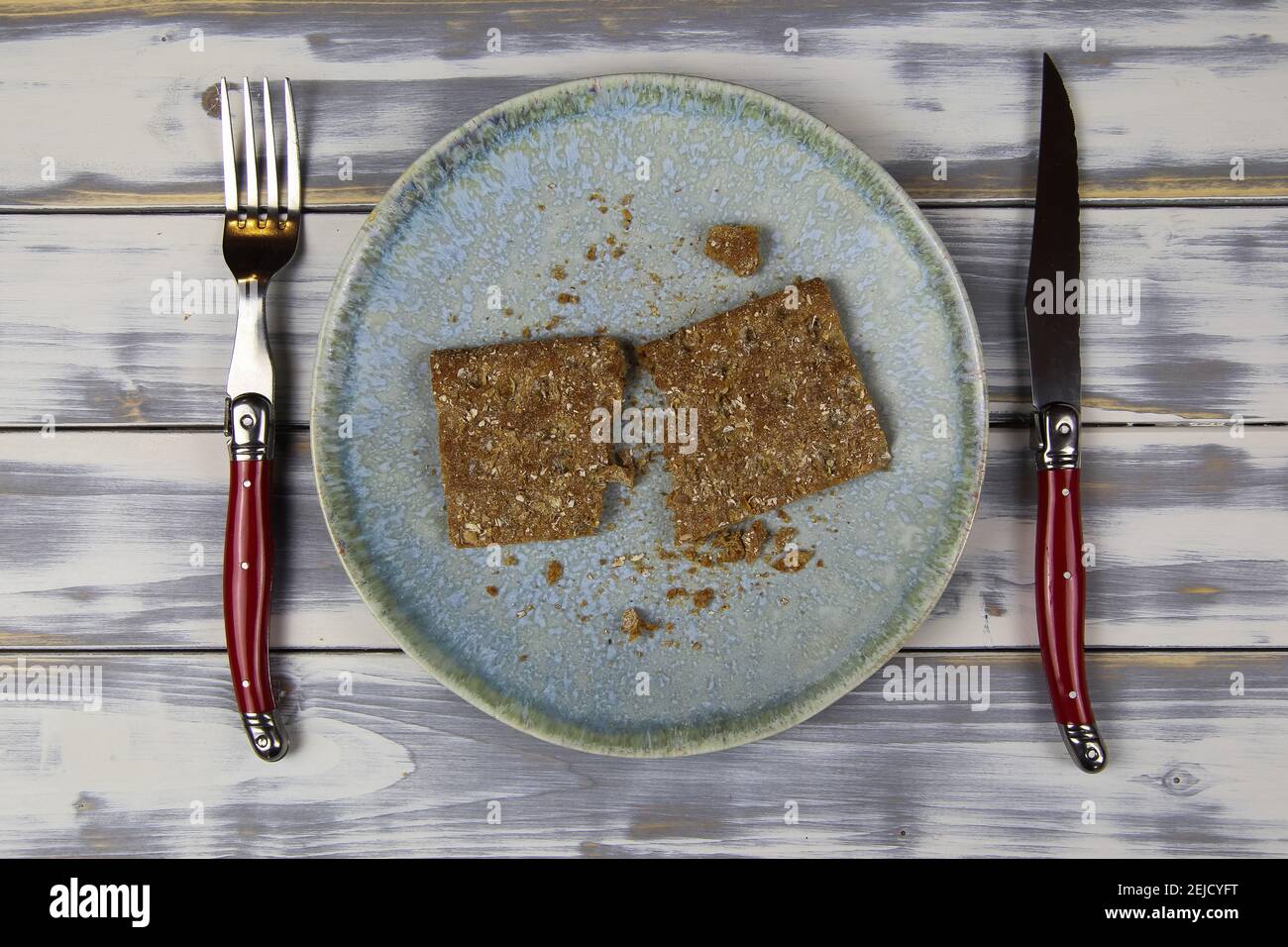 Top view on dish with one disc dry broken crispbread crumbs, cutlery on ...