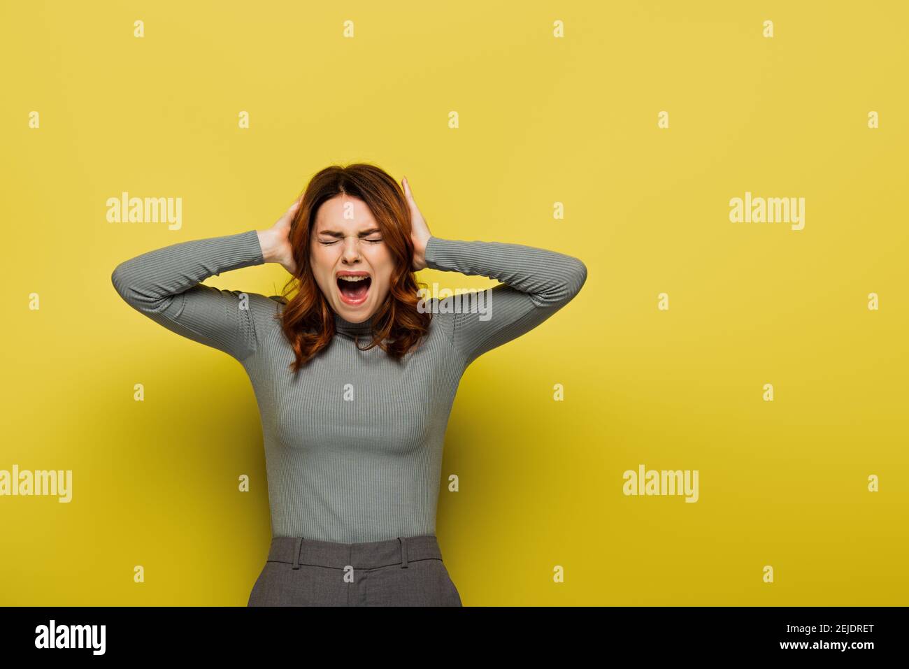 young woman screaming while touching head on yellow Stock Photo - Alamy