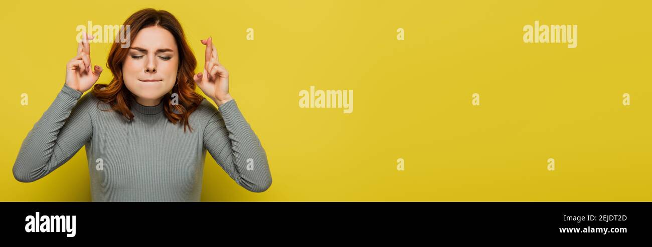 tense woman with crossed fingers standing with closed eyes on yellow ...