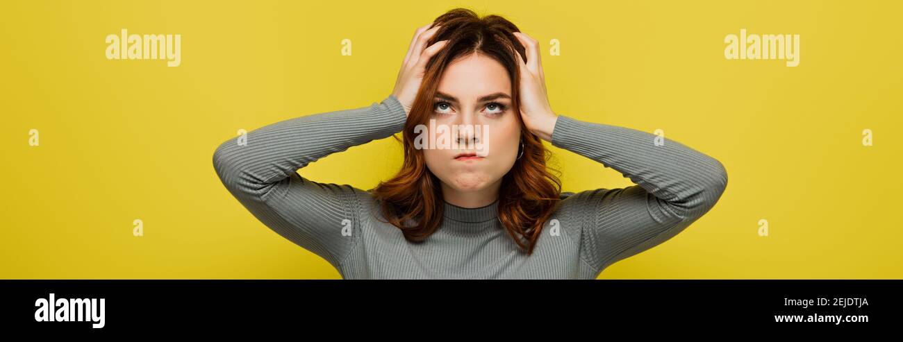 irritated woman looking up while touching head isolated on yellow ...