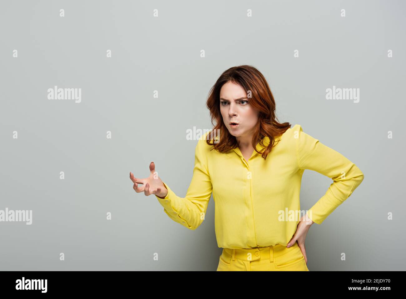 angry woman showing frightening gesture while standing with hand on hip ...