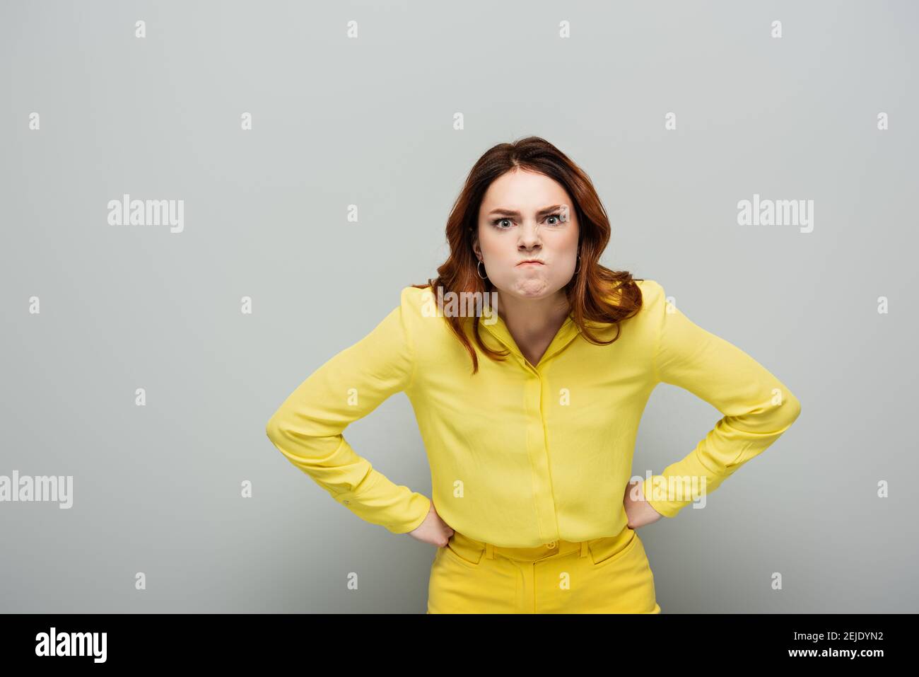 irritated woman puffing cheeks while standing with hands on hips on ...