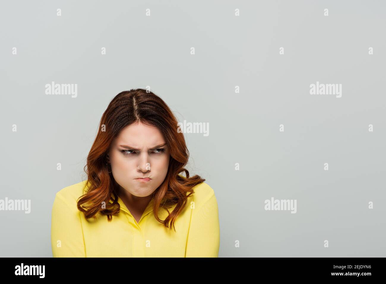 irritated woman puffing cheeks while looking away on grey Stock Photo ...
