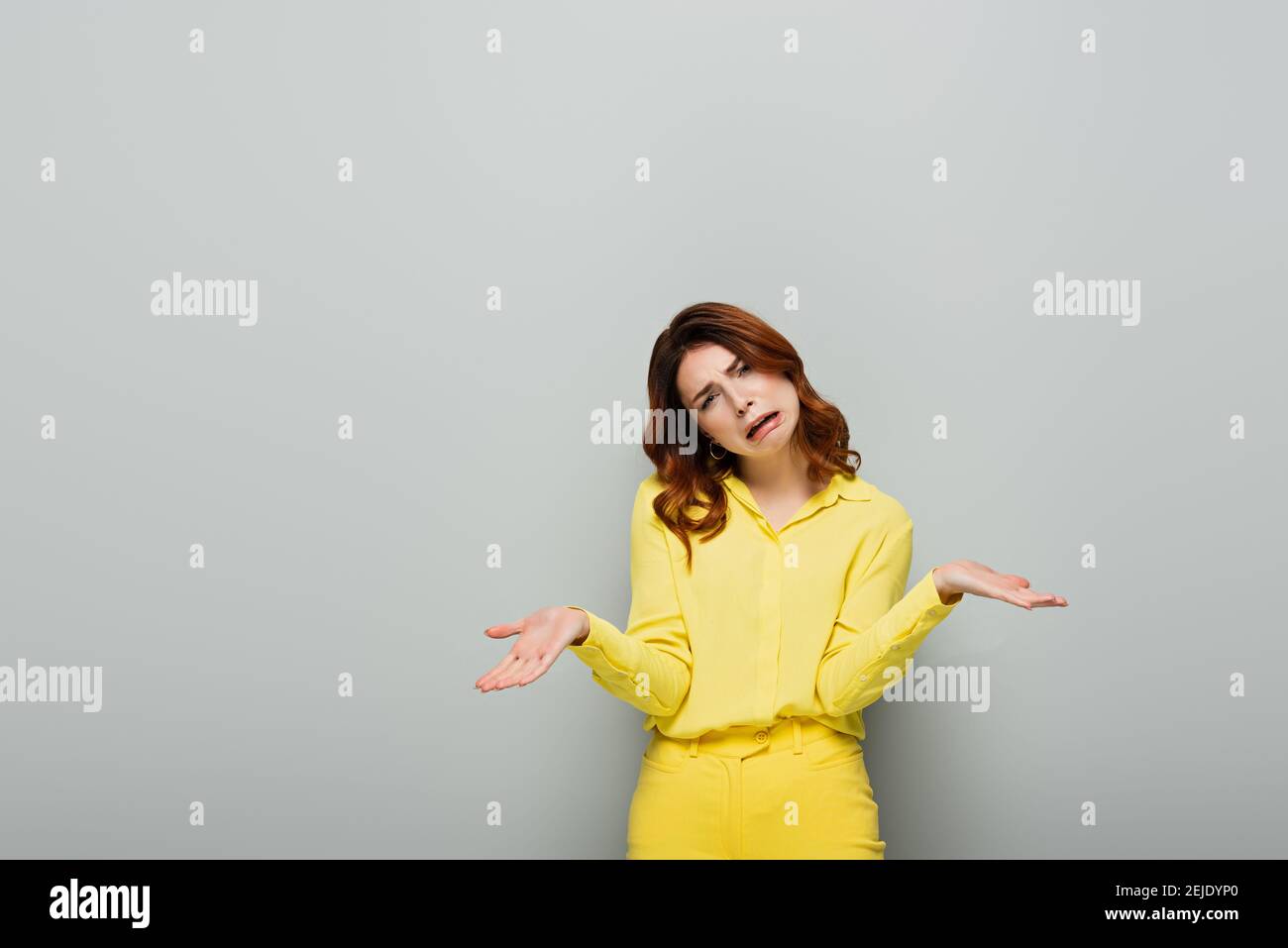 upset woman showing shrug gesture while looking at camera on grey Stock ...