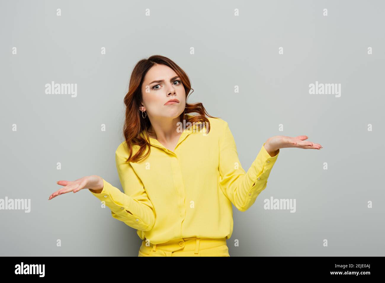 confused woman looking at camera while showing shrug gesture on grey ...